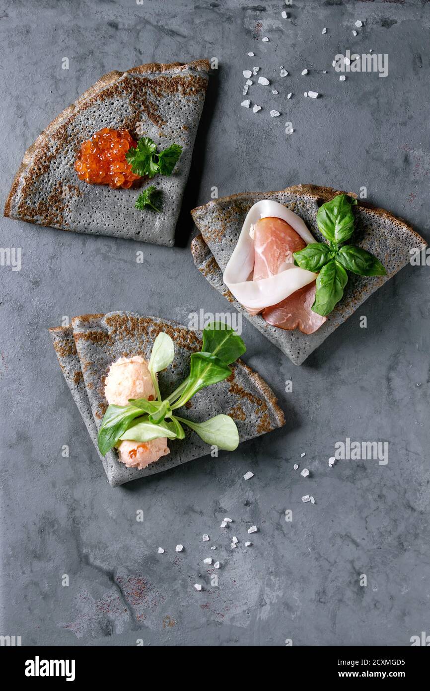 Black pancakes crepes with variety of salt filling red caviar, ham ...