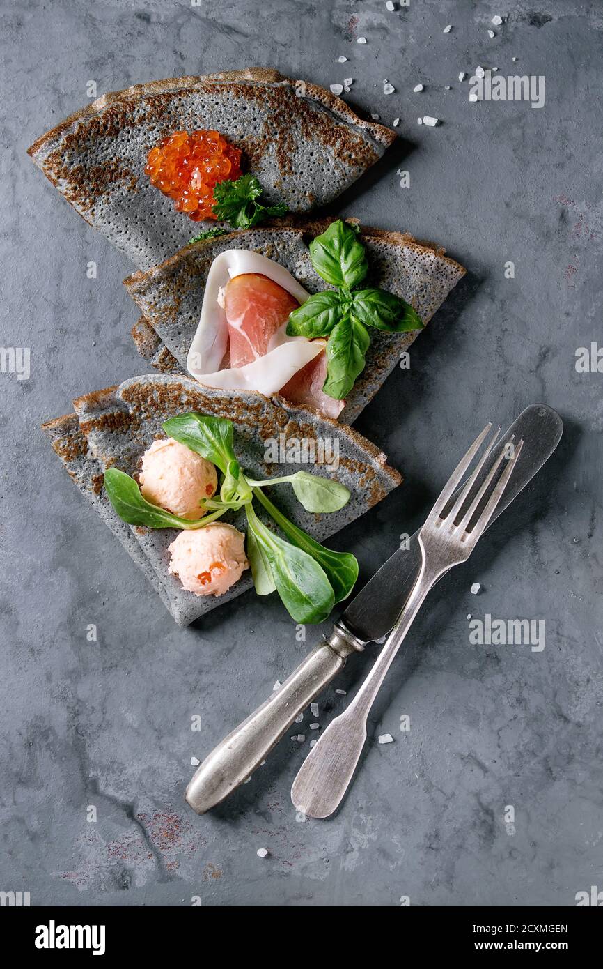 Black pancakes crepes with variety of salt filling red caviar, ham ...