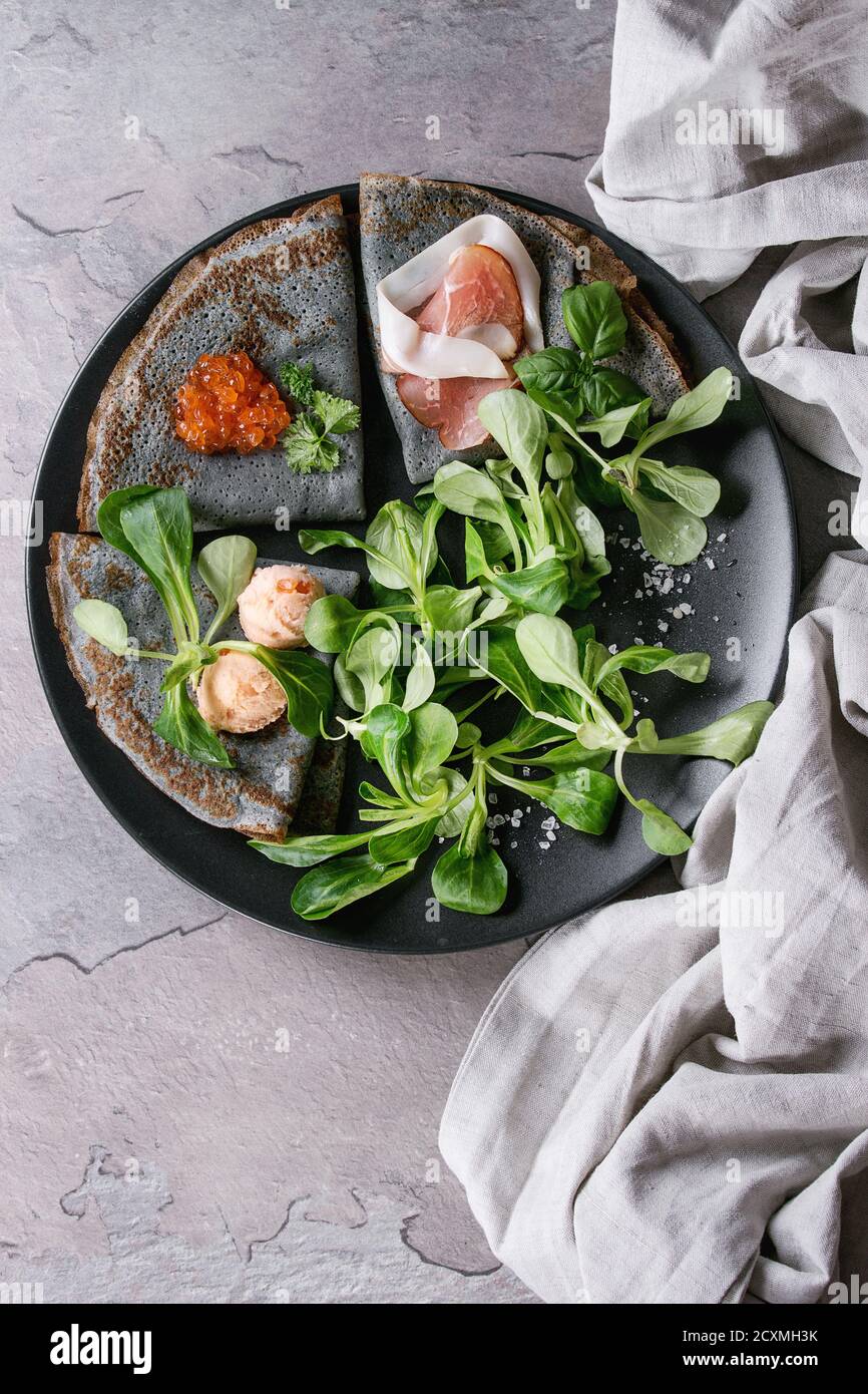 Black pancakes crepes with variety of salt filling red caviar, ham ...