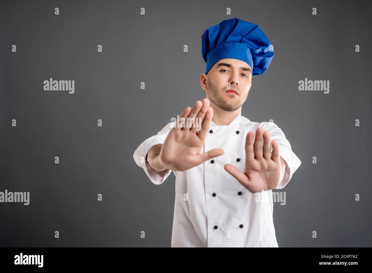Portrait of young male dressed in a white chef suit showing stop sign ...