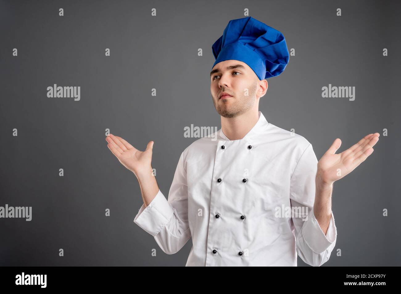 Portrait of young male dressed in a white chef suit with open arms ...