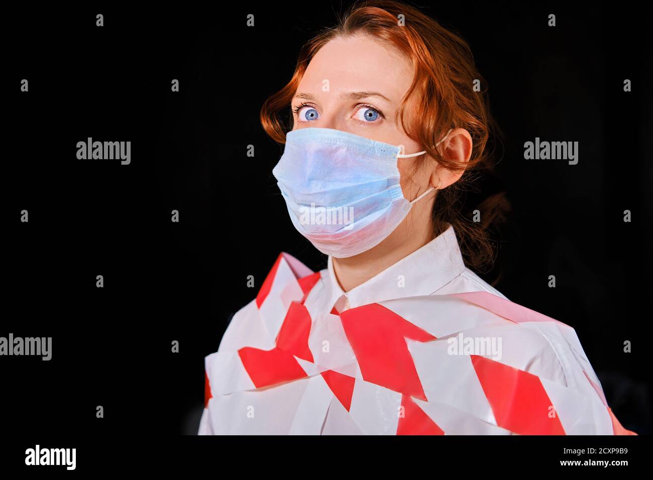 Tied woman with scared eyes in medical mask on a black background ...