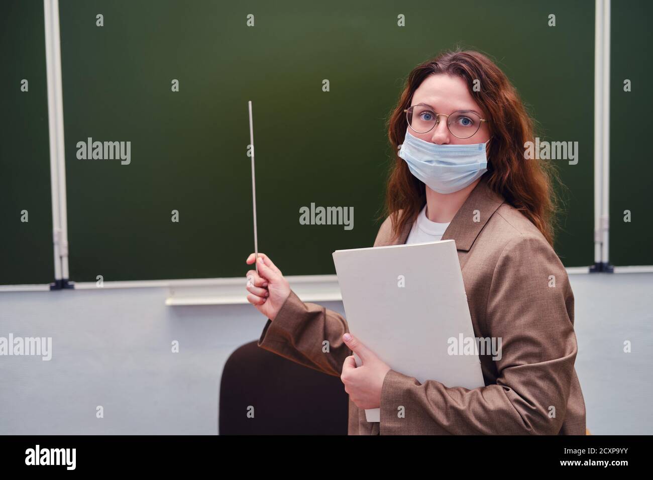 Woman teacher with pointer on the background of the school blackboard ...