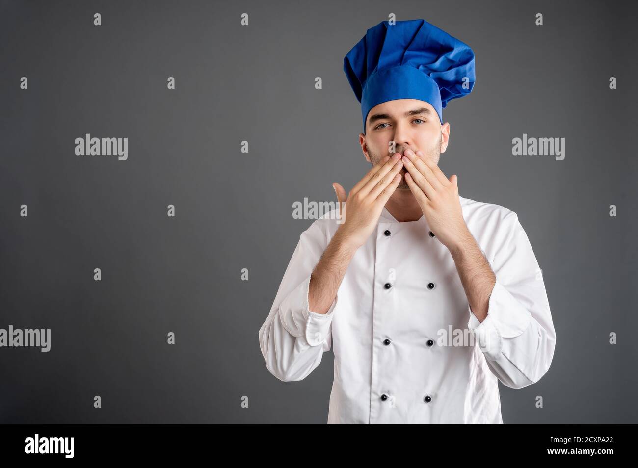 Portrait of young male dressed in a white chef suit covering mouth like ...