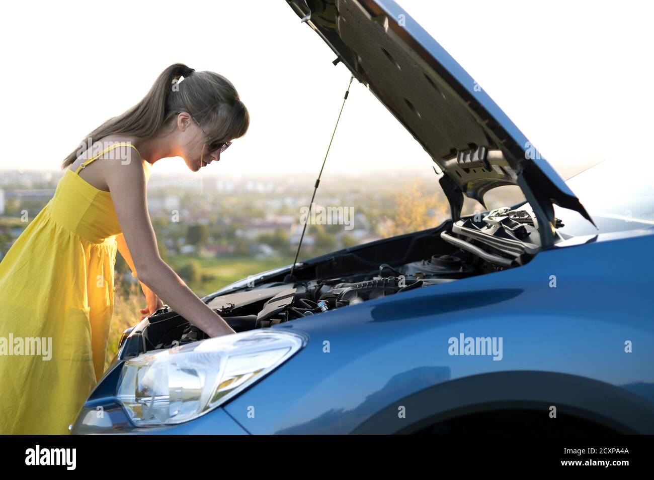 Puzzled woman driver standing near her car with popped up hood ...