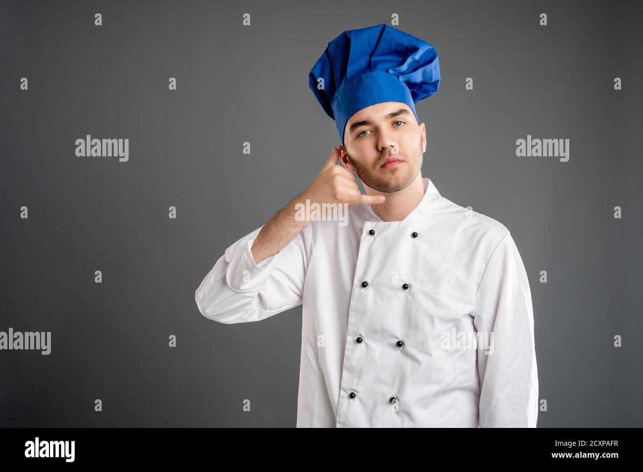 Portrait of young male dressed in a white chef suit showing call me ...