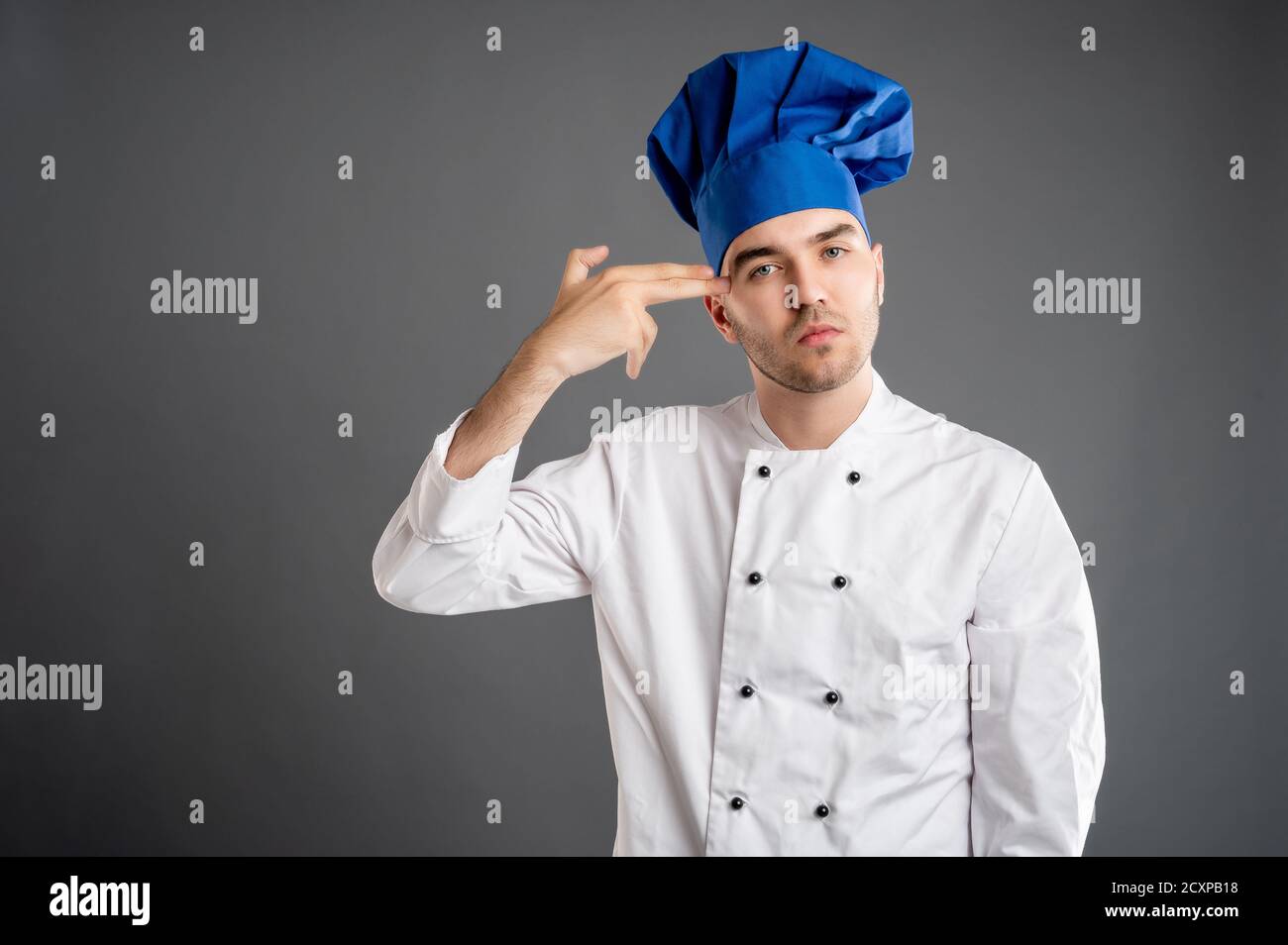Portrait of young male dressed in a white chef suit showing shot head ...