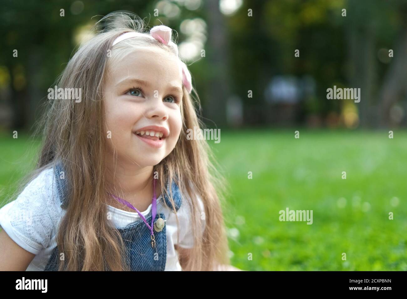 Portrait of pretty child girl in sitting in summer park smiling happily ...
