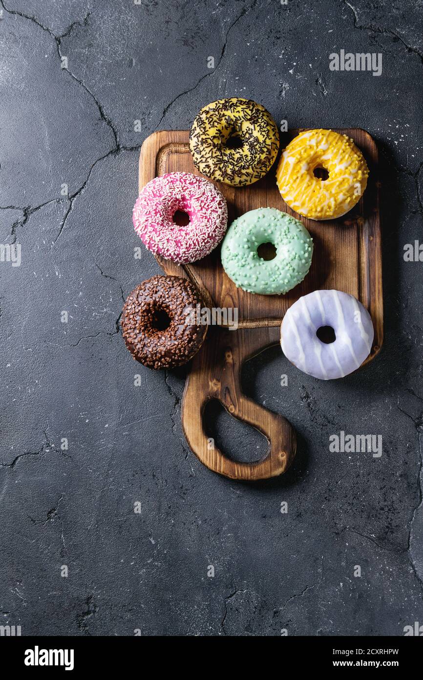 Variety of colorful glazed donuts on wooden serving board over black ...