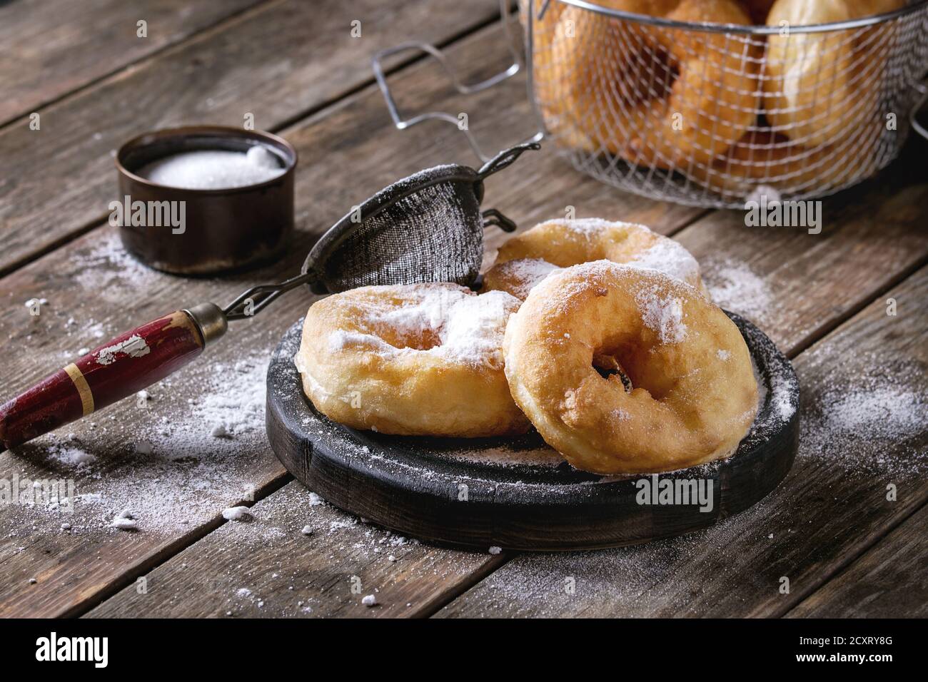 Homemade donuts with sugar powder on black serving board and in frying ...
