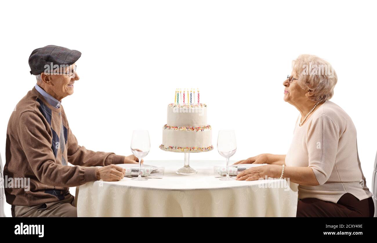 Elderly couple celebrating with a birthday cake at a table isolated on ...