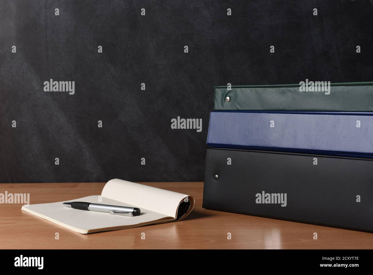Teachers desk with note pad and pen and a stack of different colored ...
