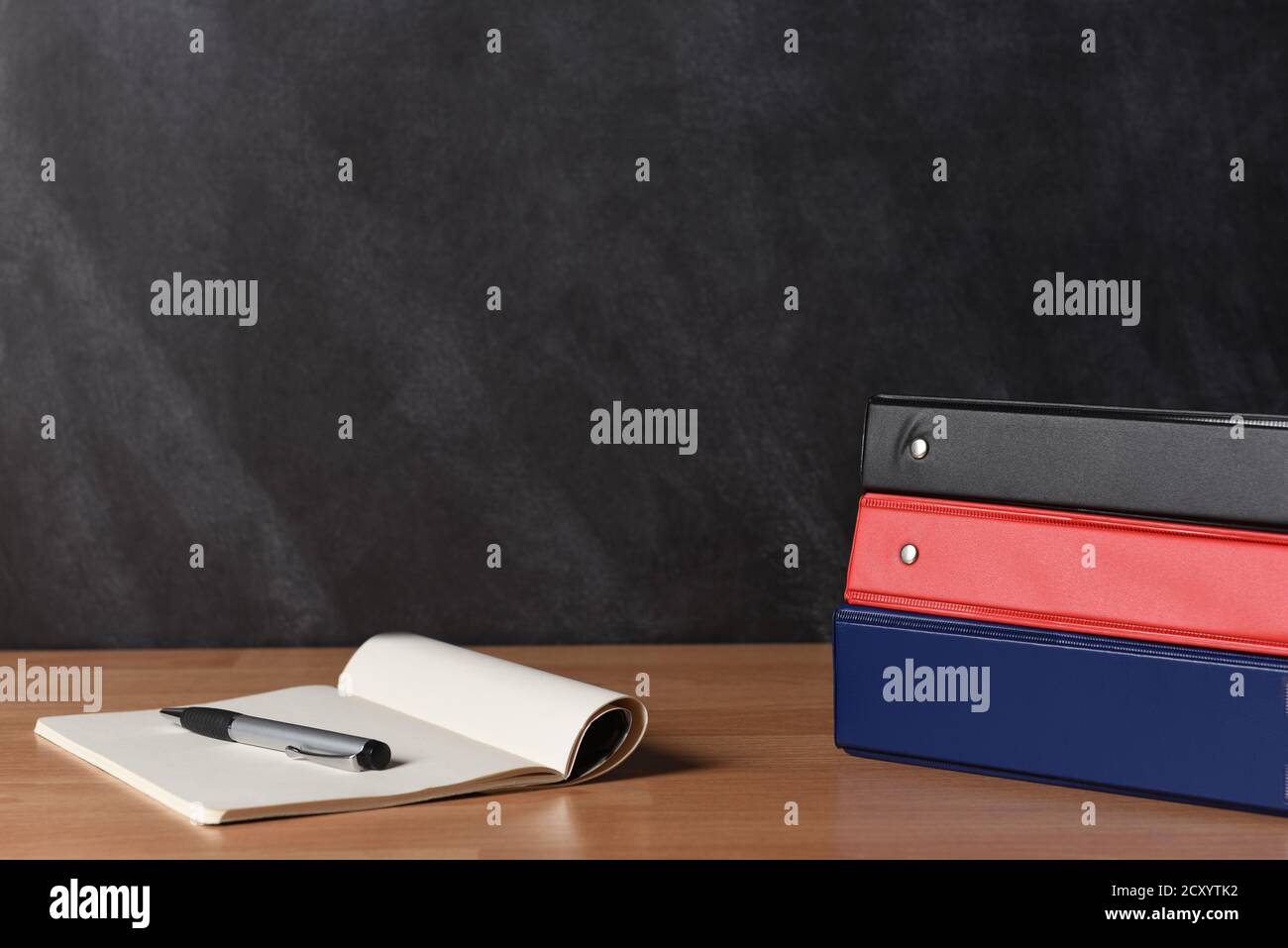 Three different binders with note pad and pen laying on a teachers desk ...