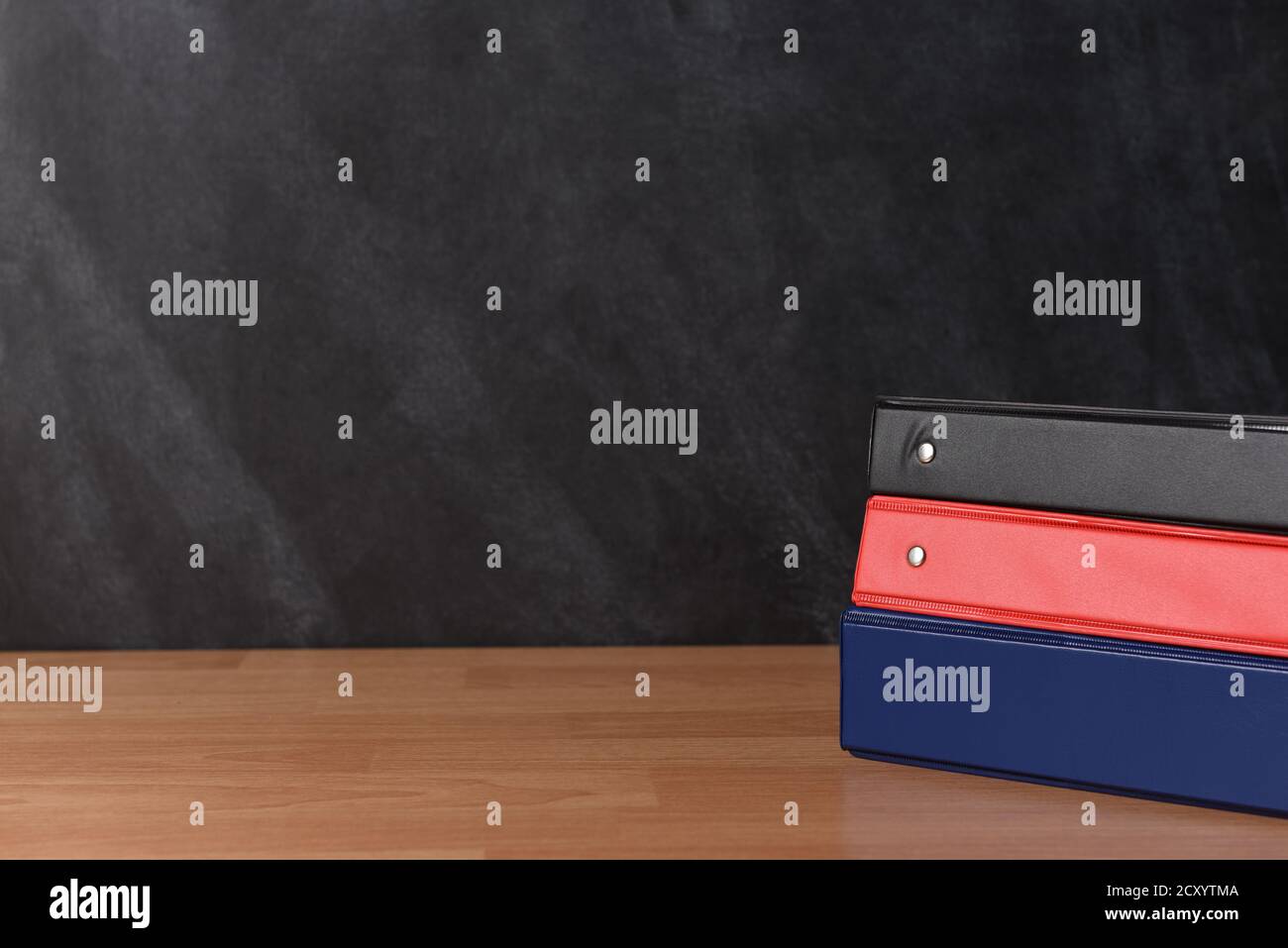 Three different binders laying on a teachers desk in front of a chalk ...