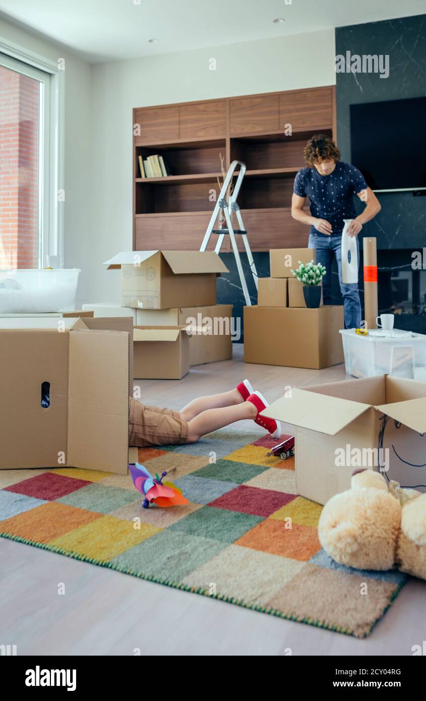 Boy playing inside a moving box while his father unpacks Stock Photo ...