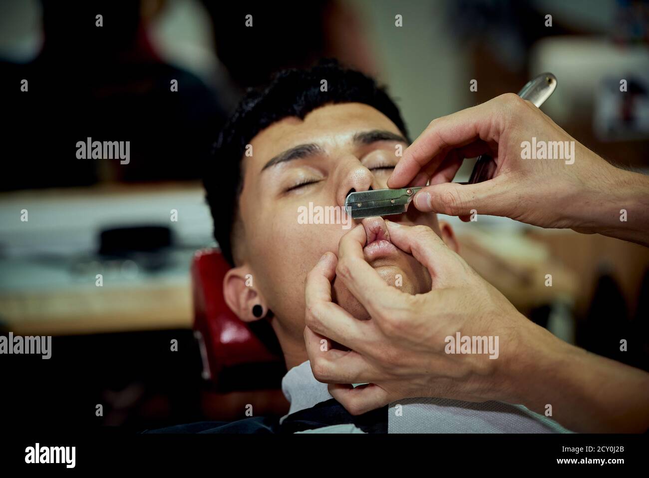 A young boy has his moustache shaved off with a razor. Barber concept ...