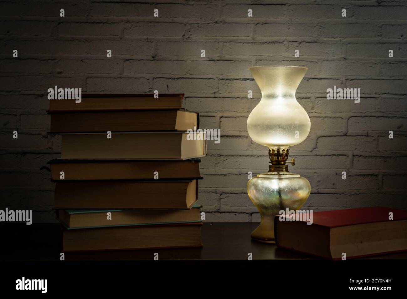 The light of an oil lamp illuminates books placed on a dark wooden ...