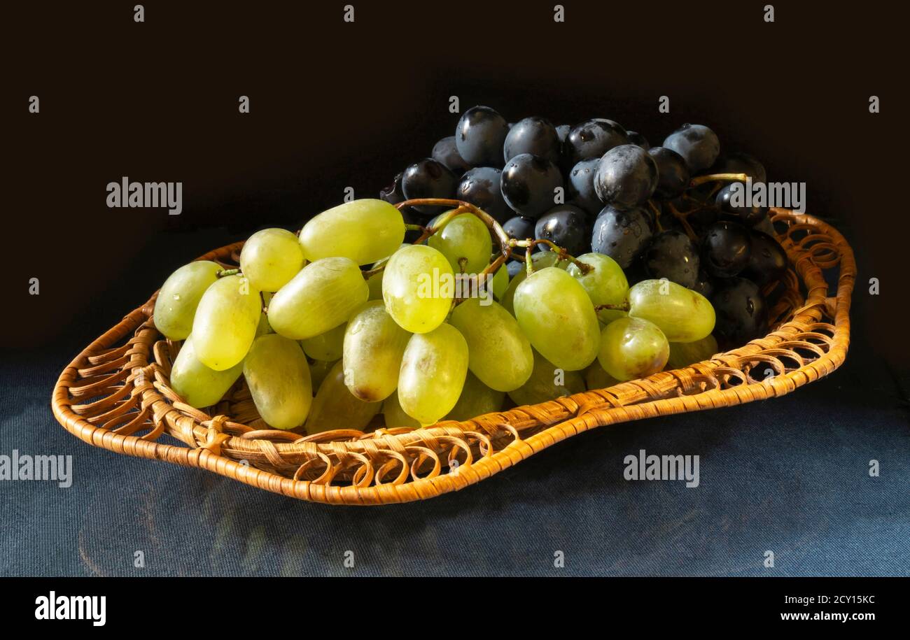 Green and dark grape in plate on table on dark background. Ripe berries ...
