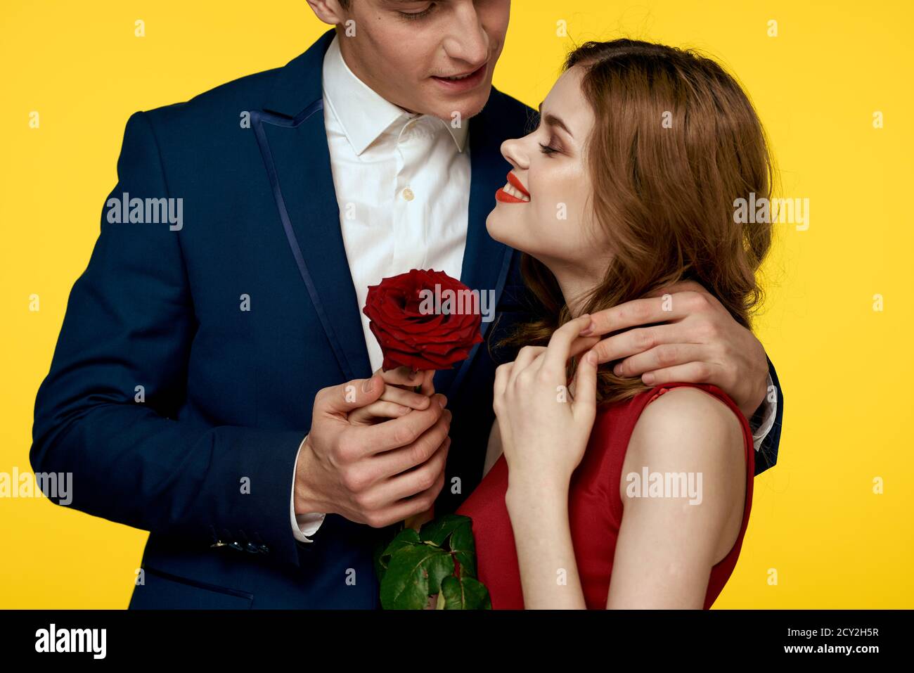 A romantic man hugs a woman in a red dress with a rose in his hand on a ...