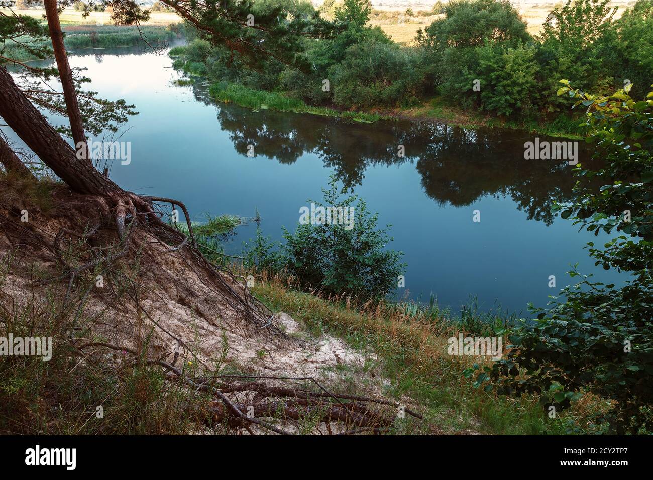 A steep cliff near a forest river flowing through a meadow against a ...