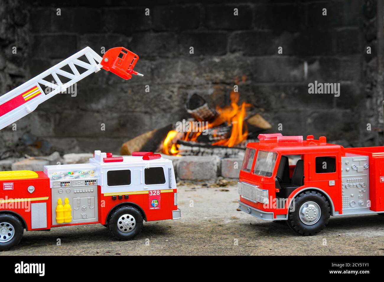 Toy red firetrucks "help out" at a real fire in an outdoor fireplace ...