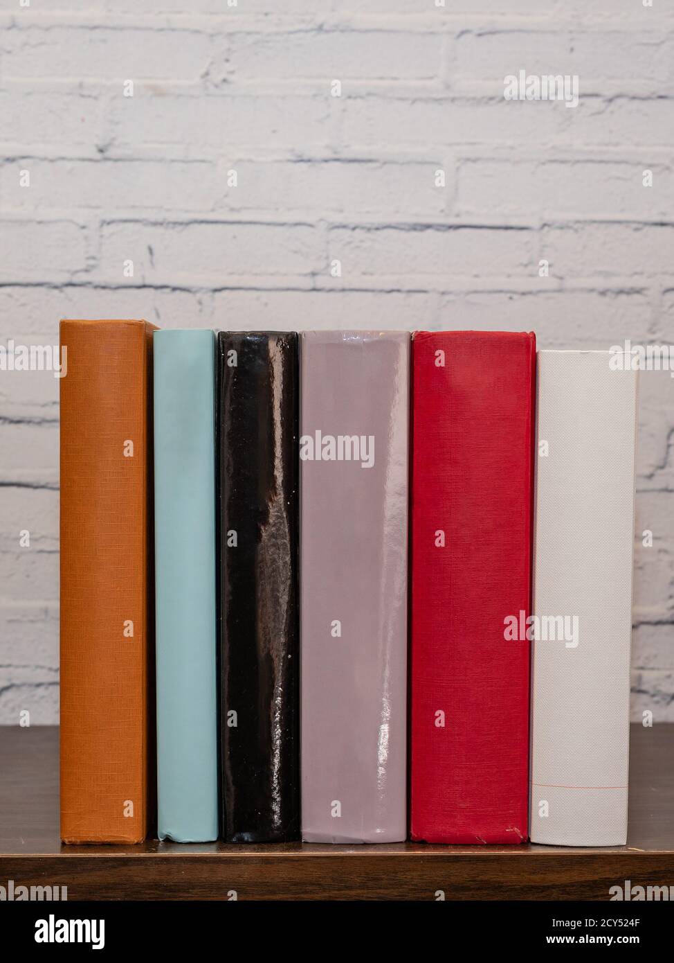 Six books of different colors resting on a dark wooden shelf, in the ...