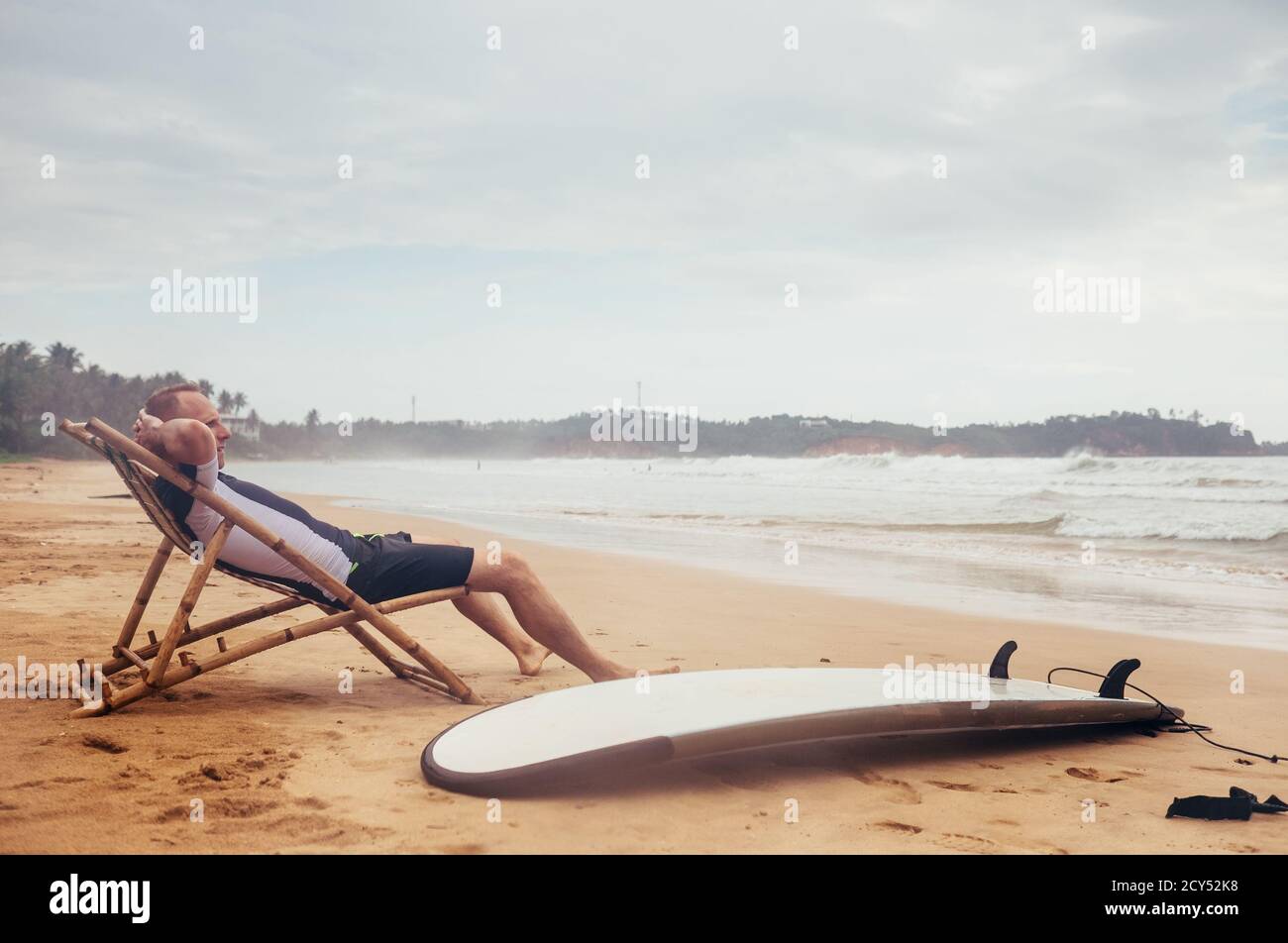 Rainy day underwater case shot of Surfer man sitting on the sandy ocean ...