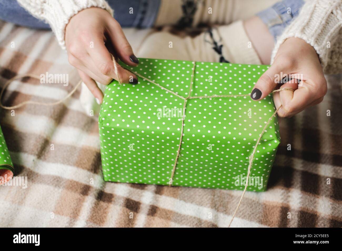 Young woman sits on plaid in cozy knitted woolen white sweater, socks ...