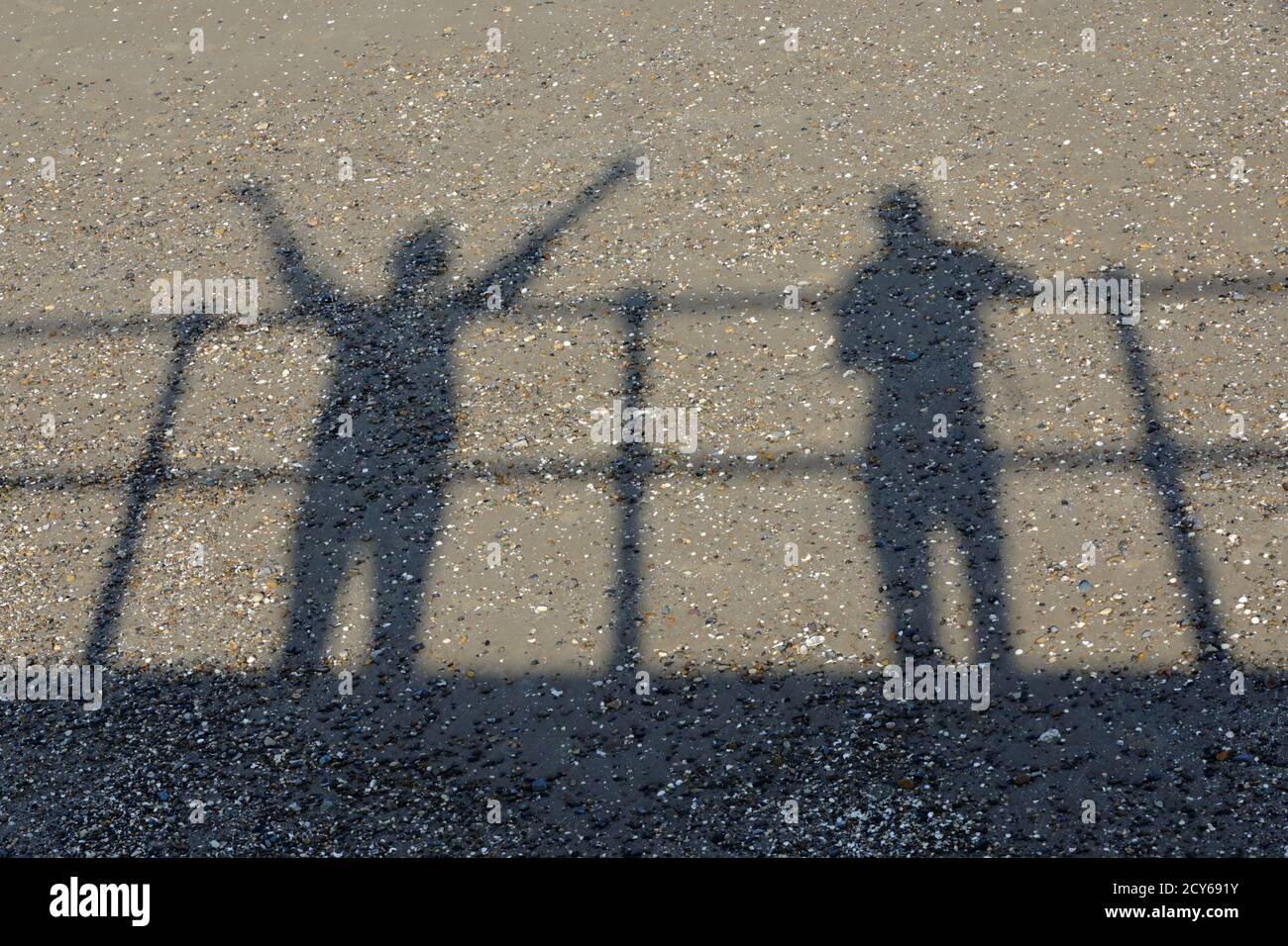 shadows of 2 people and railings cast on a beach, one shadow in the ...