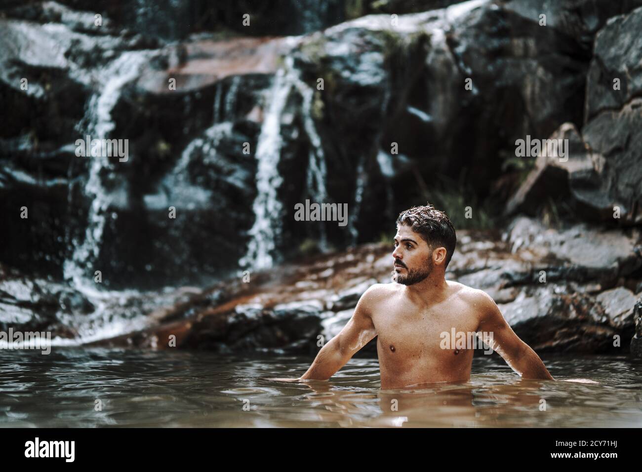 Young Caucasian male swimming in a river at a waterfall near rocks ...