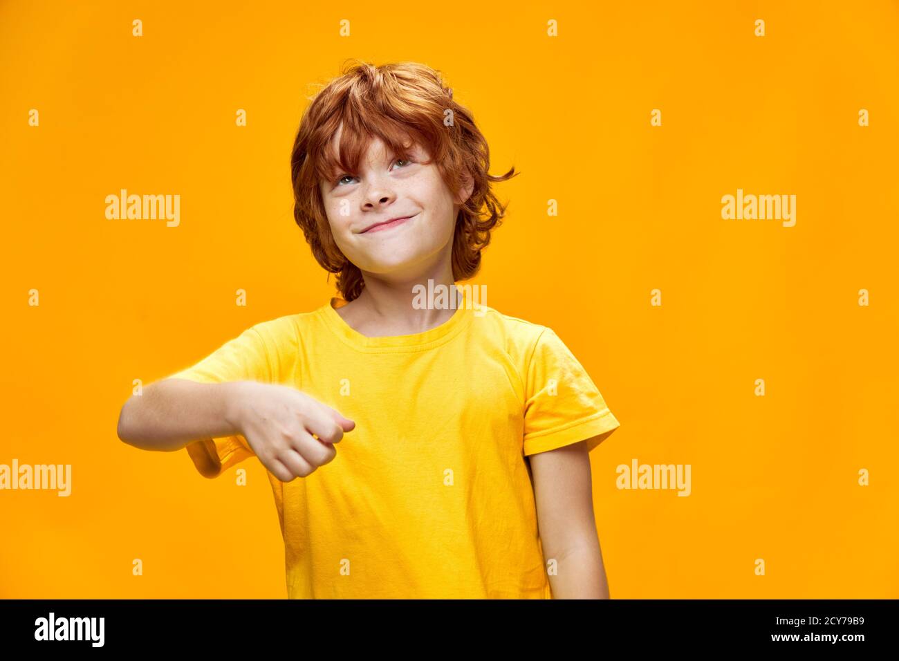 A dreamy boy with red hair on a yellow background holds his hand in ...