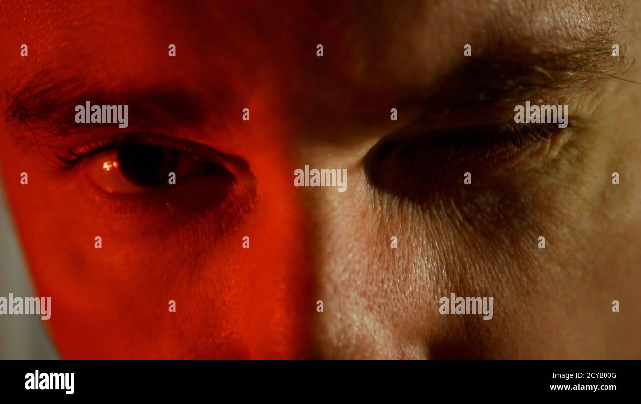 A young man with a serious look. Frowning man in red tones evil smile ...
