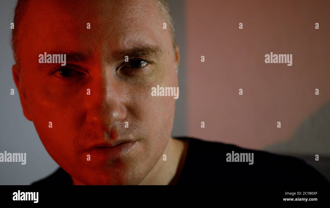 A young man with a serious look. Frowning man in red tones evil smile ...