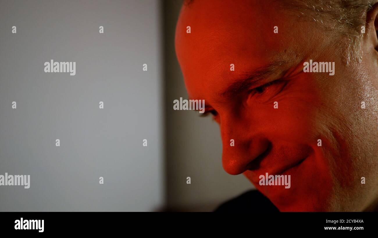 A young man with a serious look. Frowning man in red tones evil smile ...