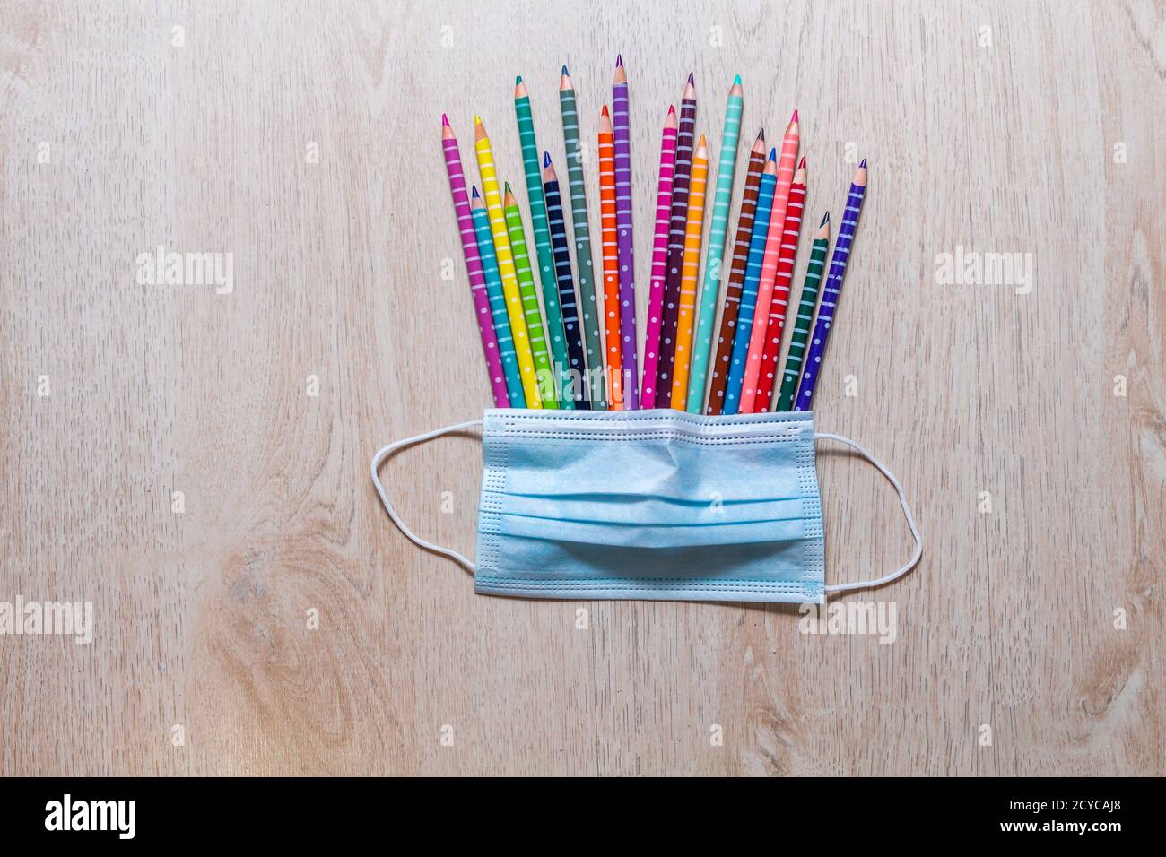 Colored pencils arranged on a desk under a respiratory protection mask ...