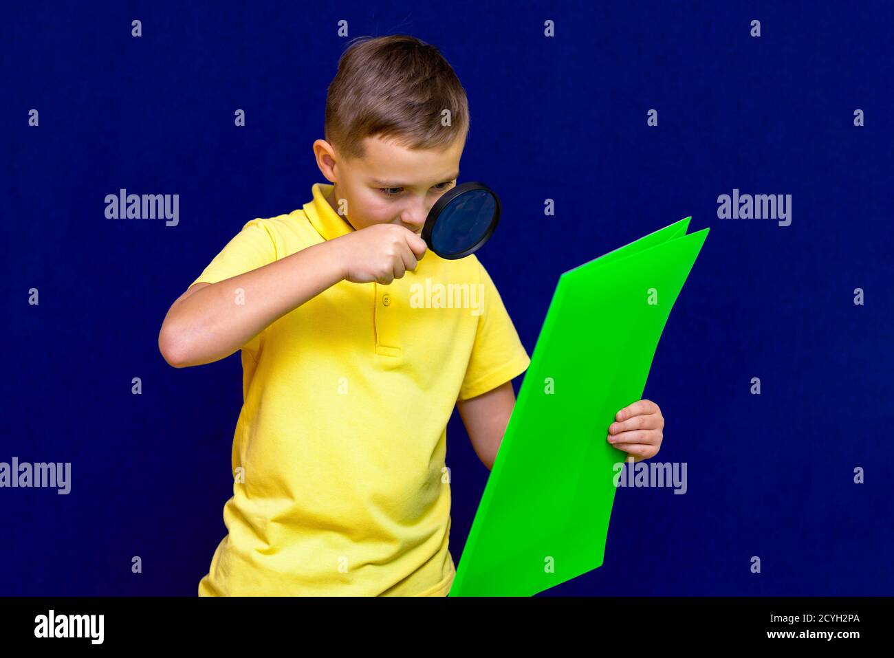 Caucasian school boy student looking at green paper using magnifying ...