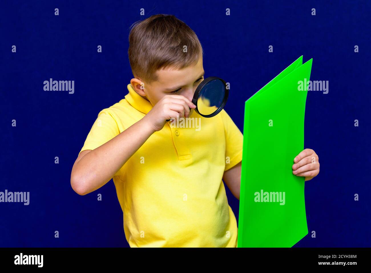 Caucasian school boy student looking at green paper using magnifying ...