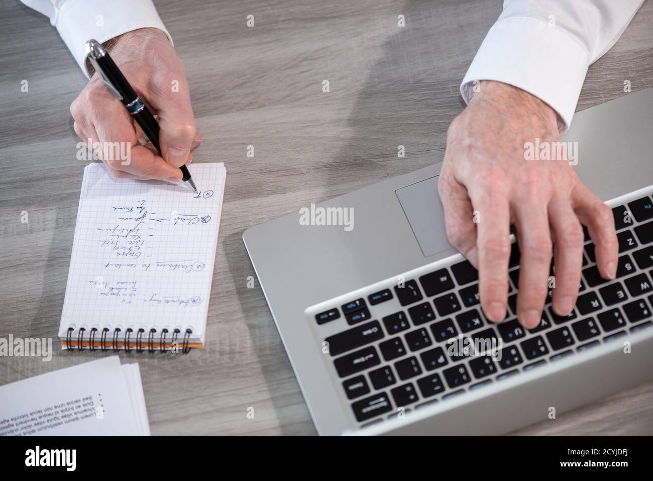Hand of businessman taking notes while using laptop Stock Photo - Alamy