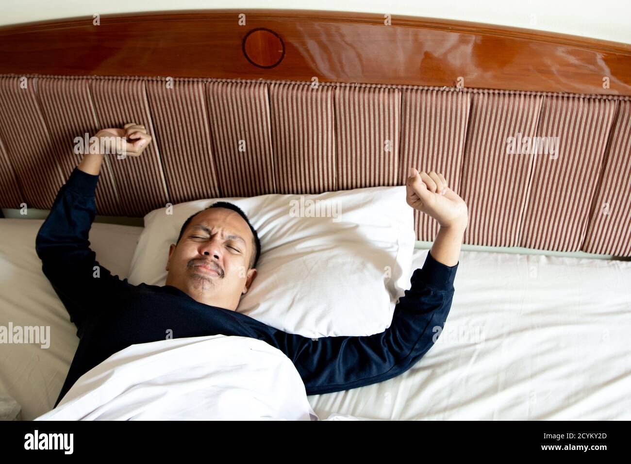 Asian man waking in morning. Asian guy stretching and yawning in bed ...