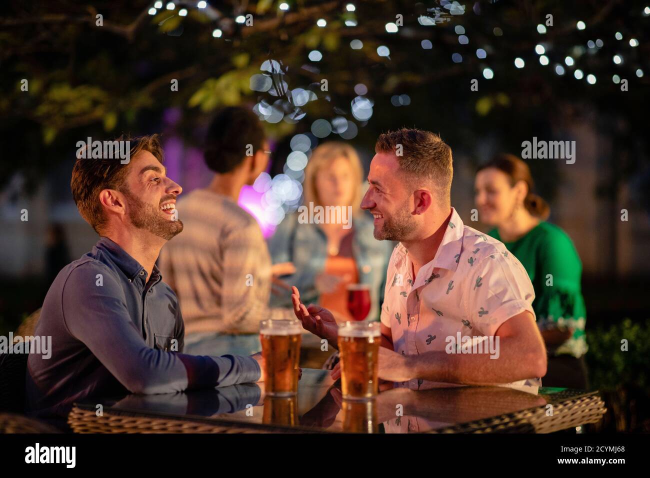LGBTQI Couple sitting down and drinking champagne outdoors at a bar ...