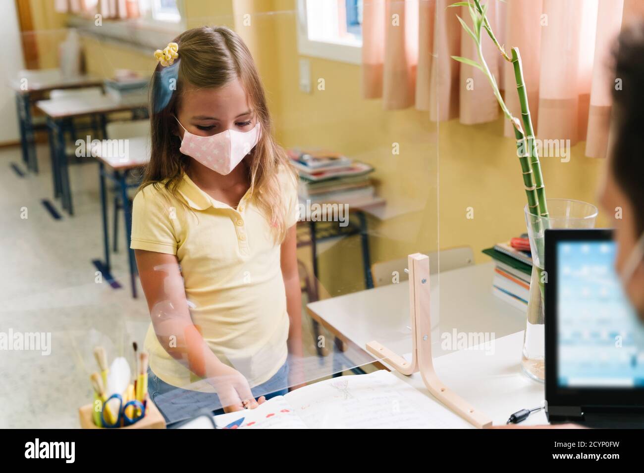 Student with a mask handing over homework to the teacher through a ...