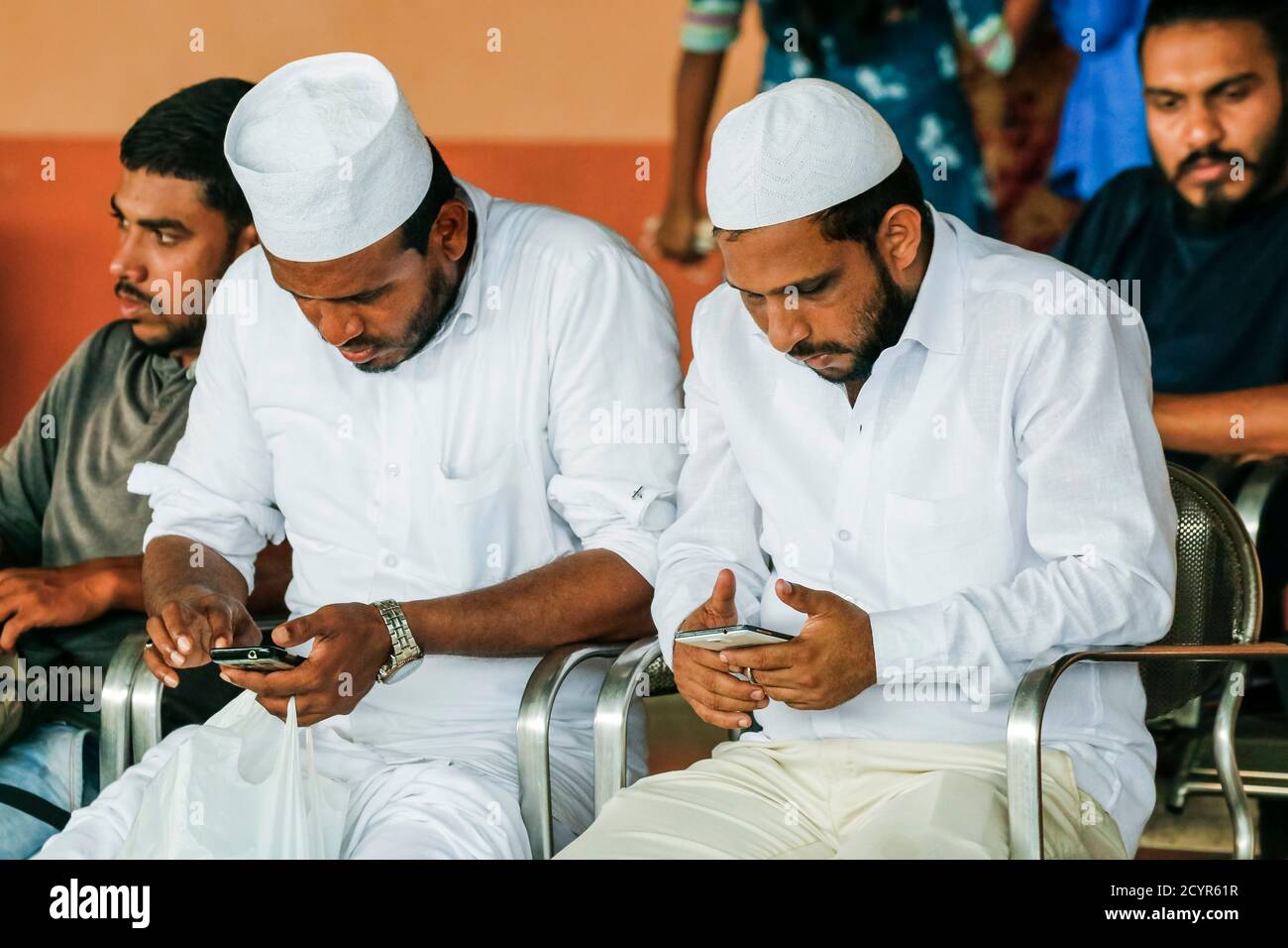 Muslim men with mobile phones & wearing taqiyah hats waiting for ...