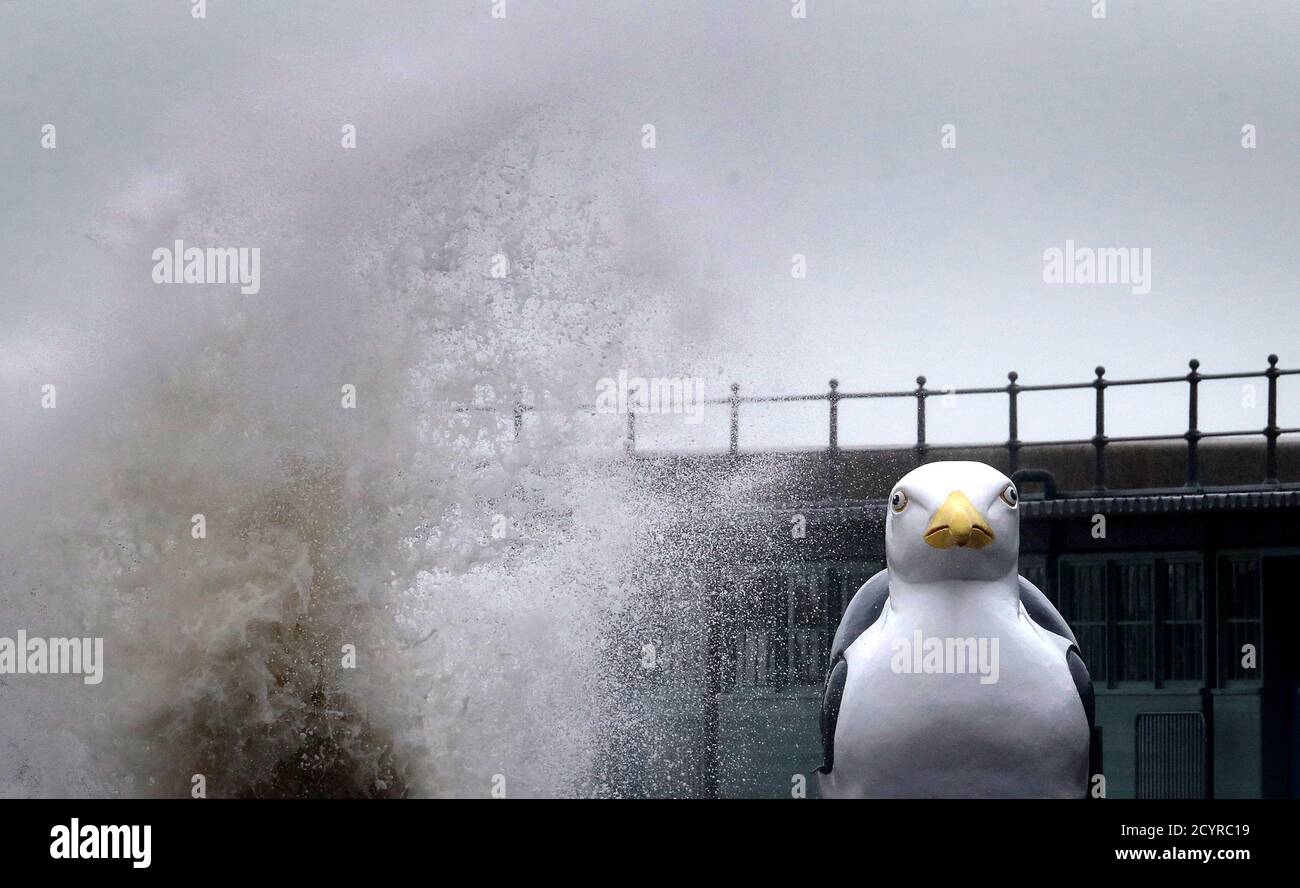 Waves crash over a model of a seagull as they hit the harbour wall in ...