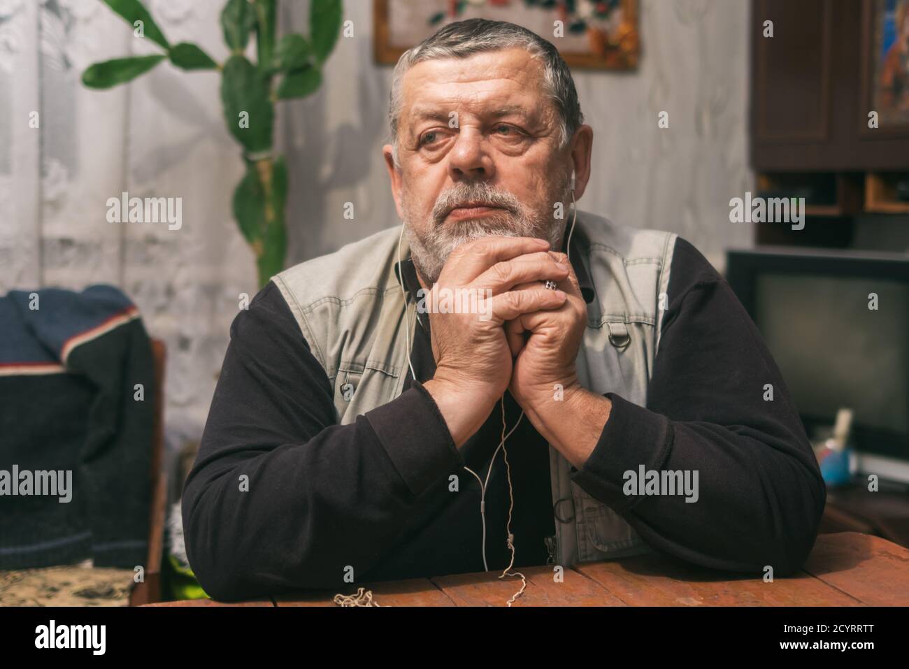 Indoor portrait of sad Ukrainian peasant sitting at wooden table and ...