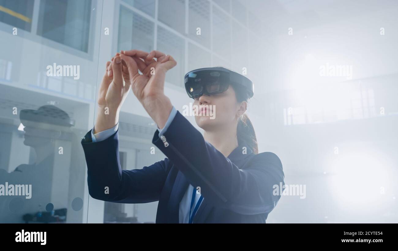 Female Engineer Using Augmented Reality Headset Making Gestures of working with Virtual Objects ...