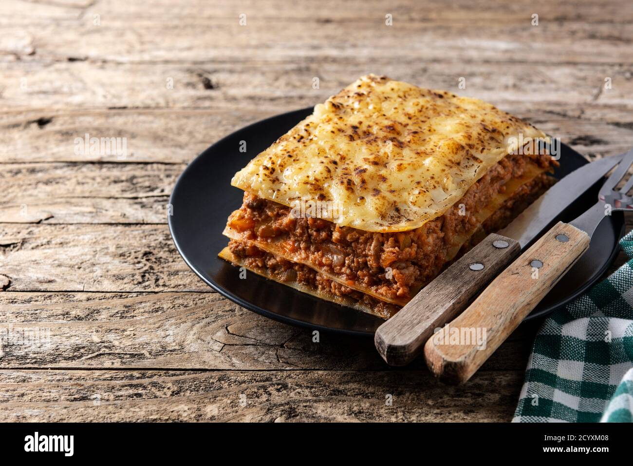 Piece of meat lasagna on black plate on rustic wooden table Stock Photo ...