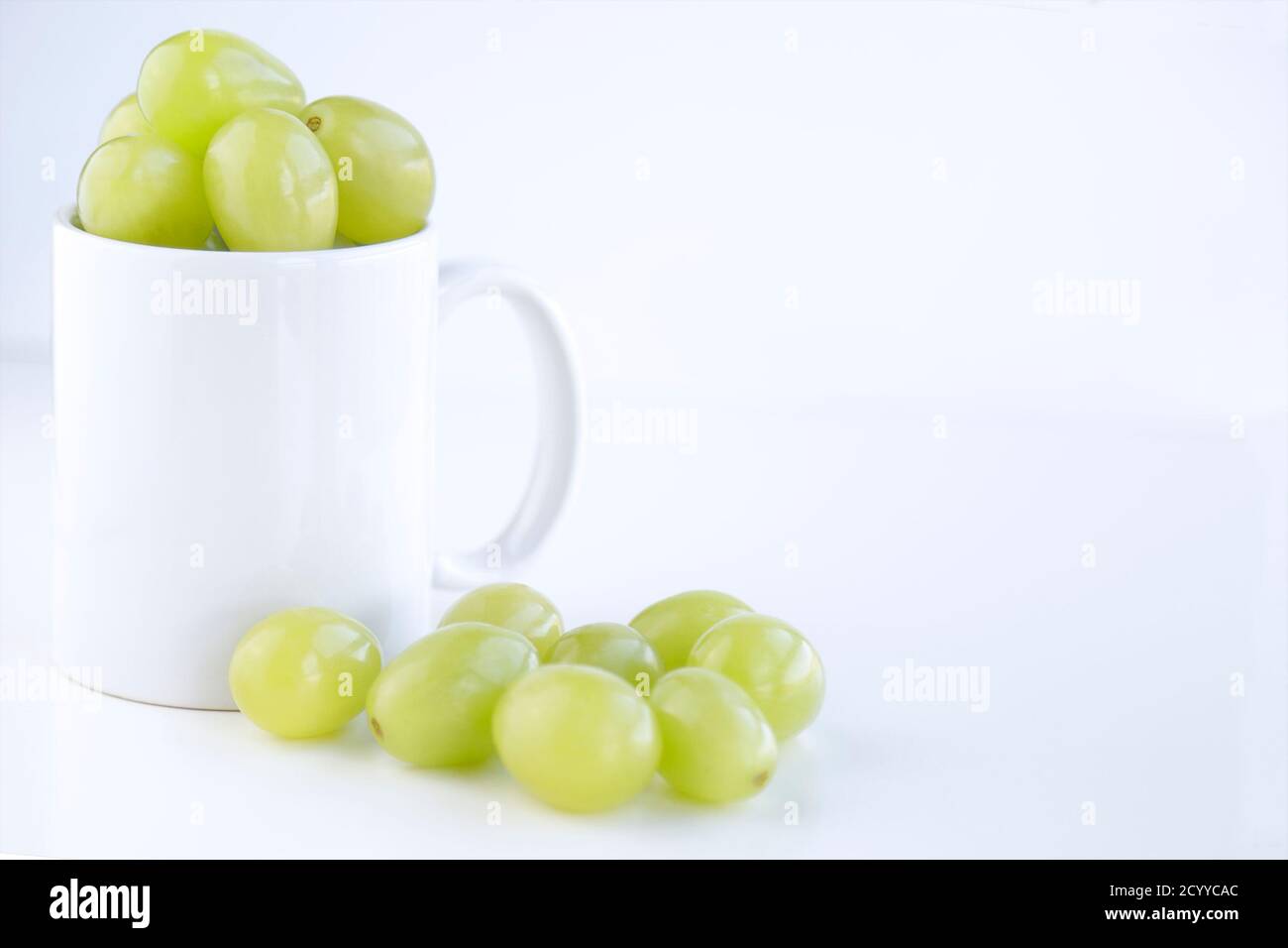 Green grapes portion inside a white mug on white background with copy ...