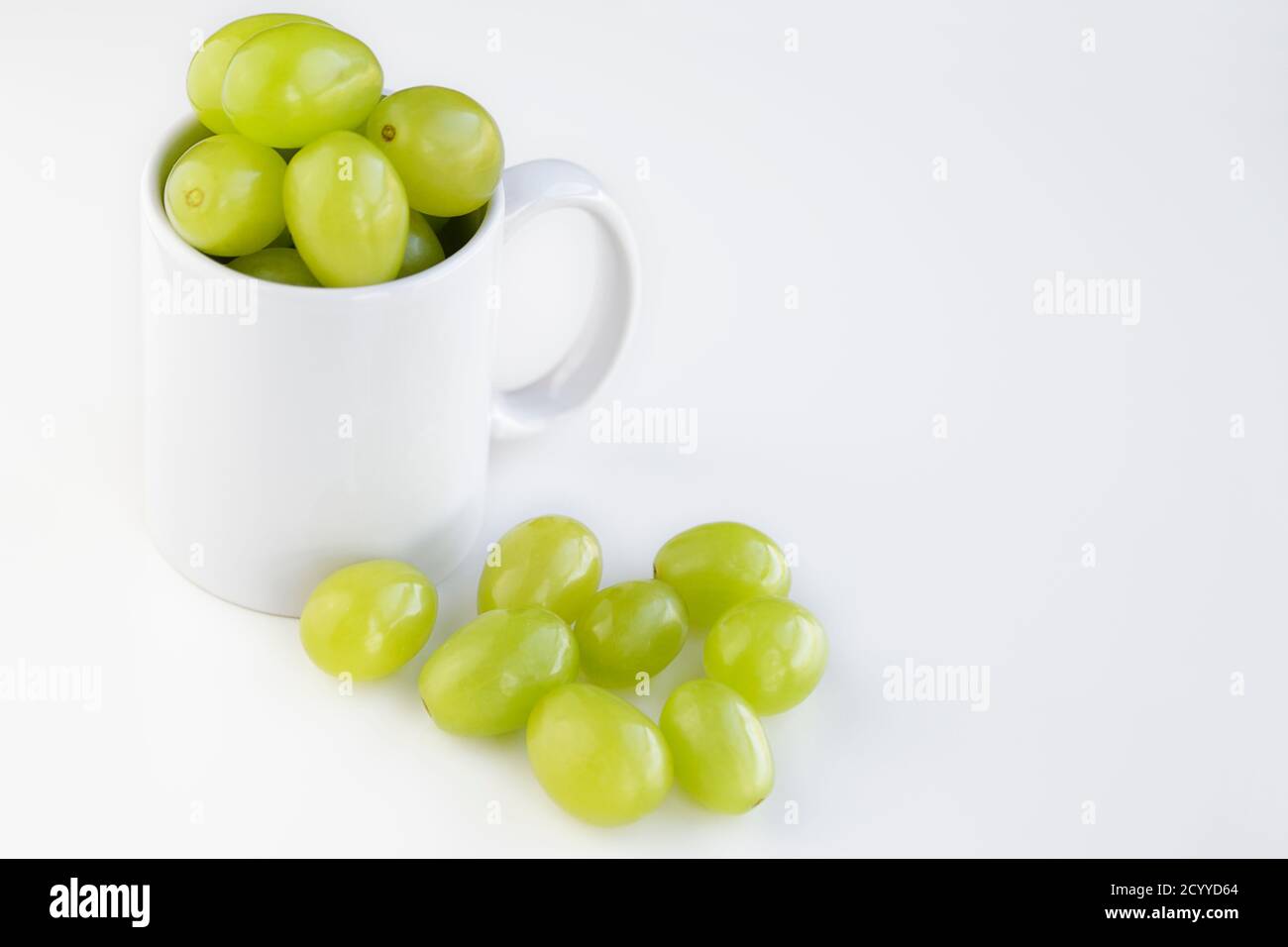 Green grapes portion inside a white mug on white background with copy ...