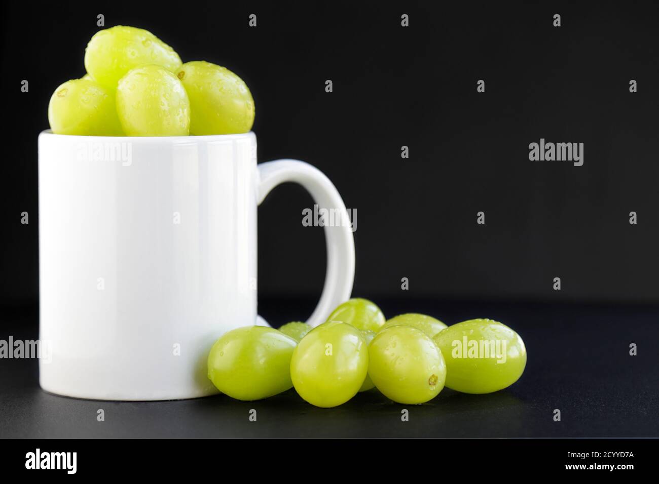 Green grapes portion inside a white mug on black background with copy ...
