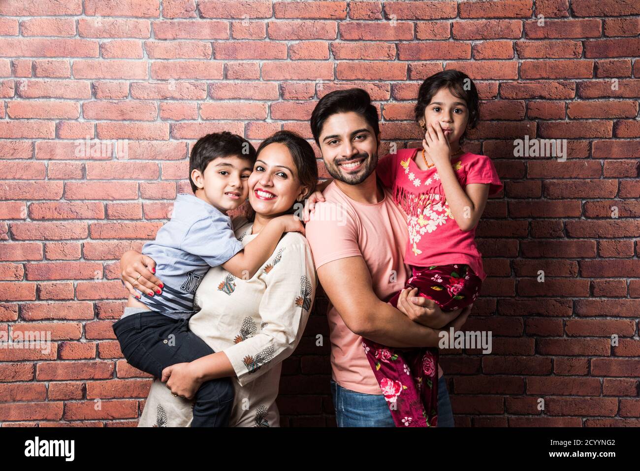 Beautiful Indian young family of four hugging, looking in camera and ...